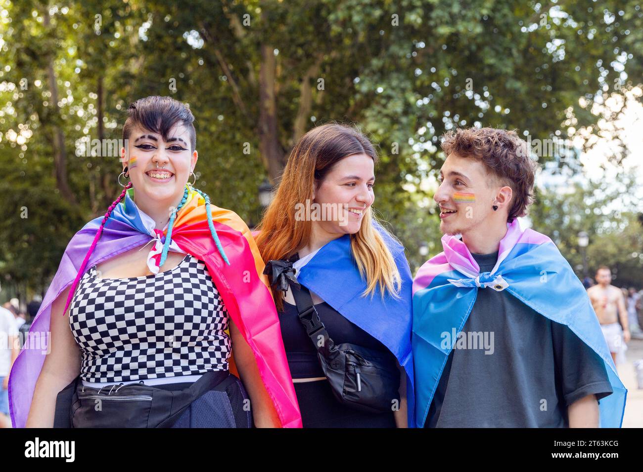 Three individuals draped in vibrant LGBTQ pride flags smiling and ...