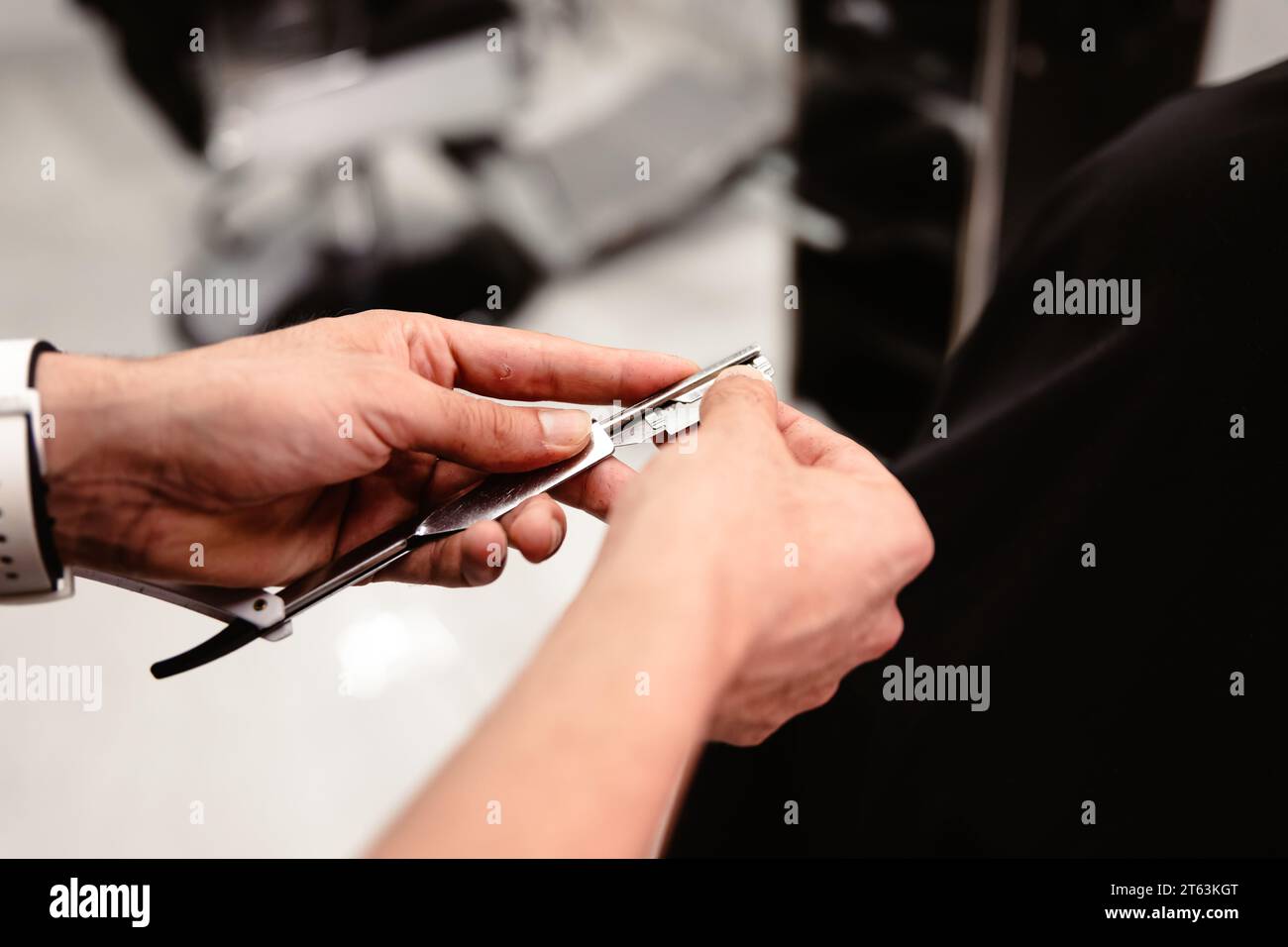 Close- up of a hairdresser's hands placing the blade on a razor to cut ...