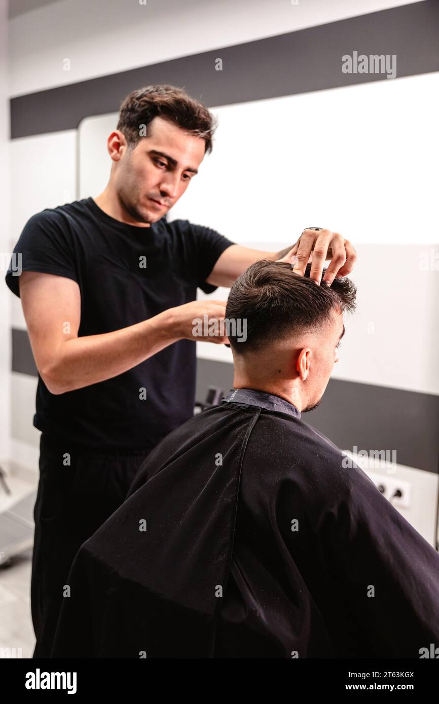 A focused barber dressed in black meticulously cutting a man's hair ...