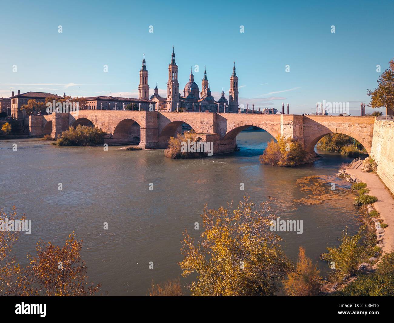 Arched stone bridge and Basilica of Nuestra Senora del Pilar over Ebro river against clear blue ...