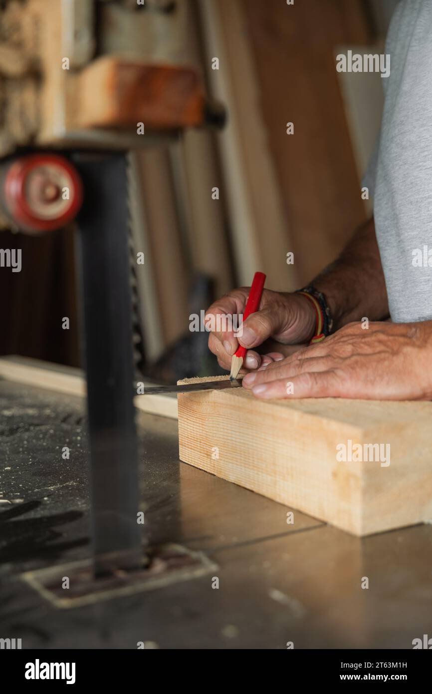 Anonymous carpenter marking a measurement on a wooden block with a red ...