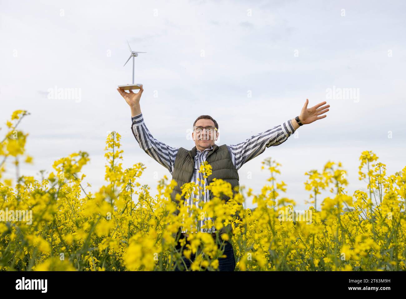 Joyful mature man with glasses raises a wind turbine model and spreads ...