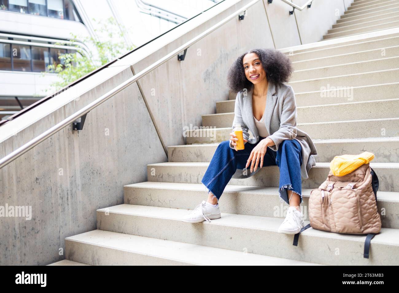 Relaxed afro woman with curly hair sitting on concrete steps outdoors ...