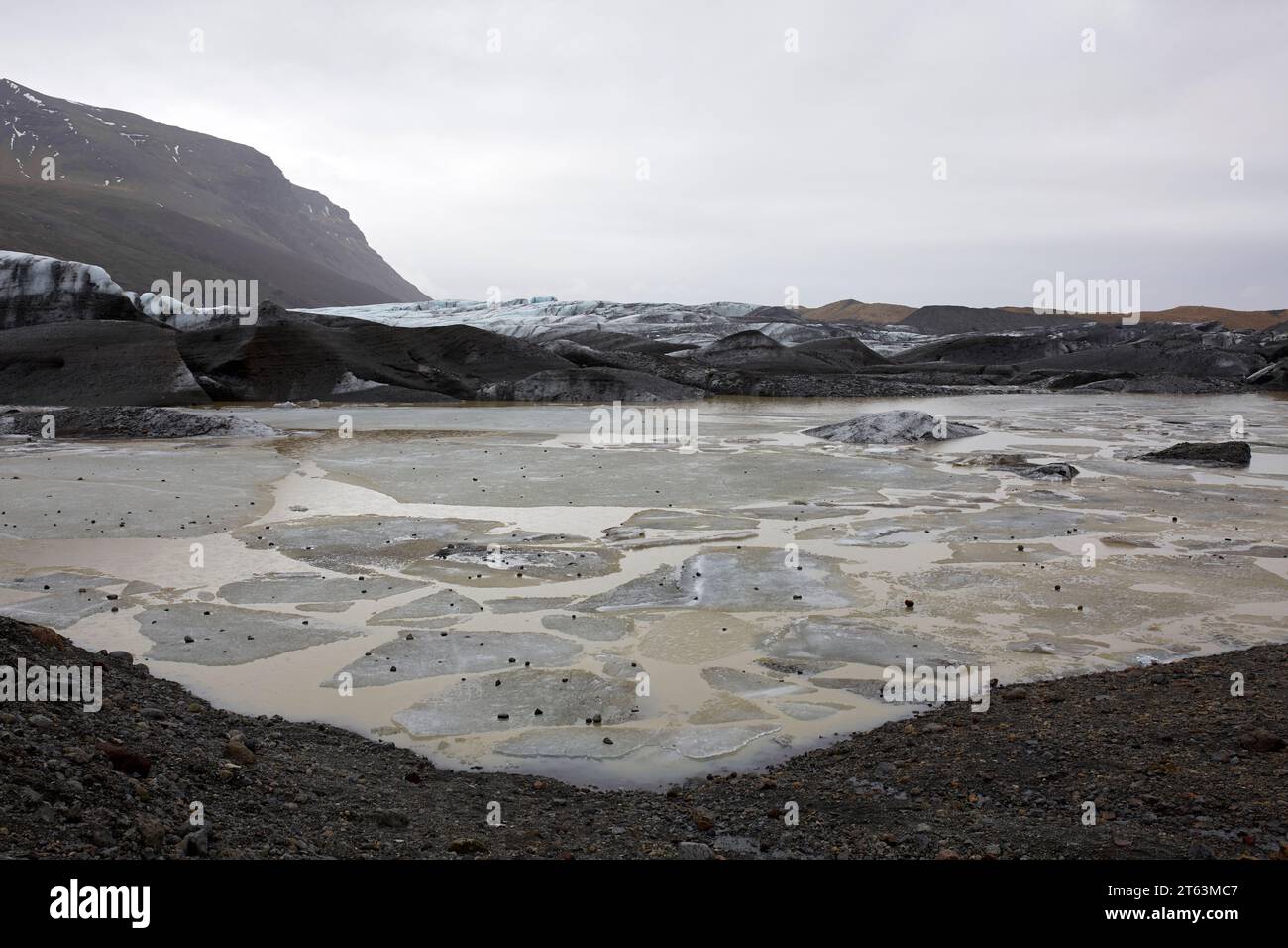Jagged ice formations arise from a murky glacial lagoon surrounded by ...