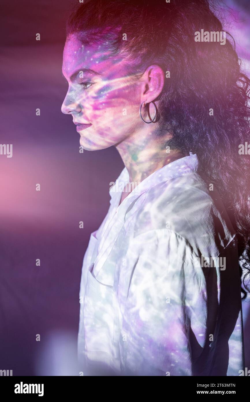 A side profile of a woman with an ethereal painted face, illuminated by ...