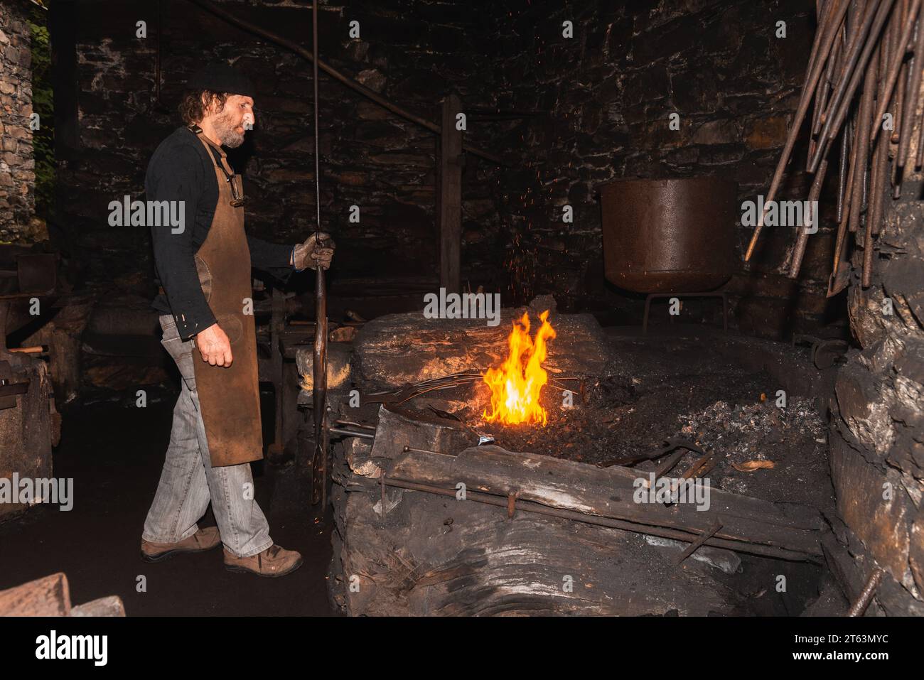Side view of dedicated blacksmith clad in a leather apron stands next ...