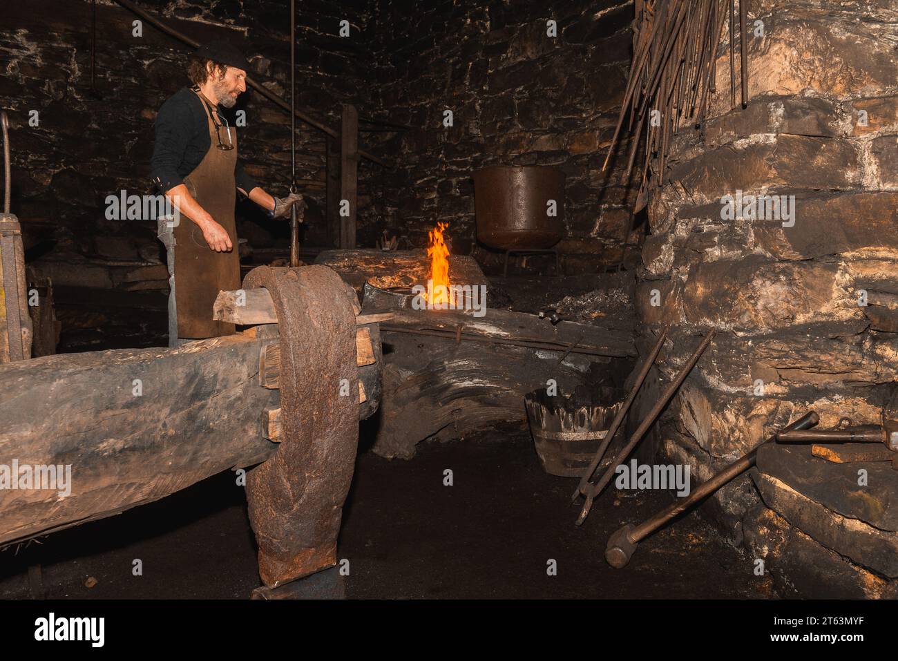 Side view of dedicated blacksmith dressed in a protective apron and hat ...