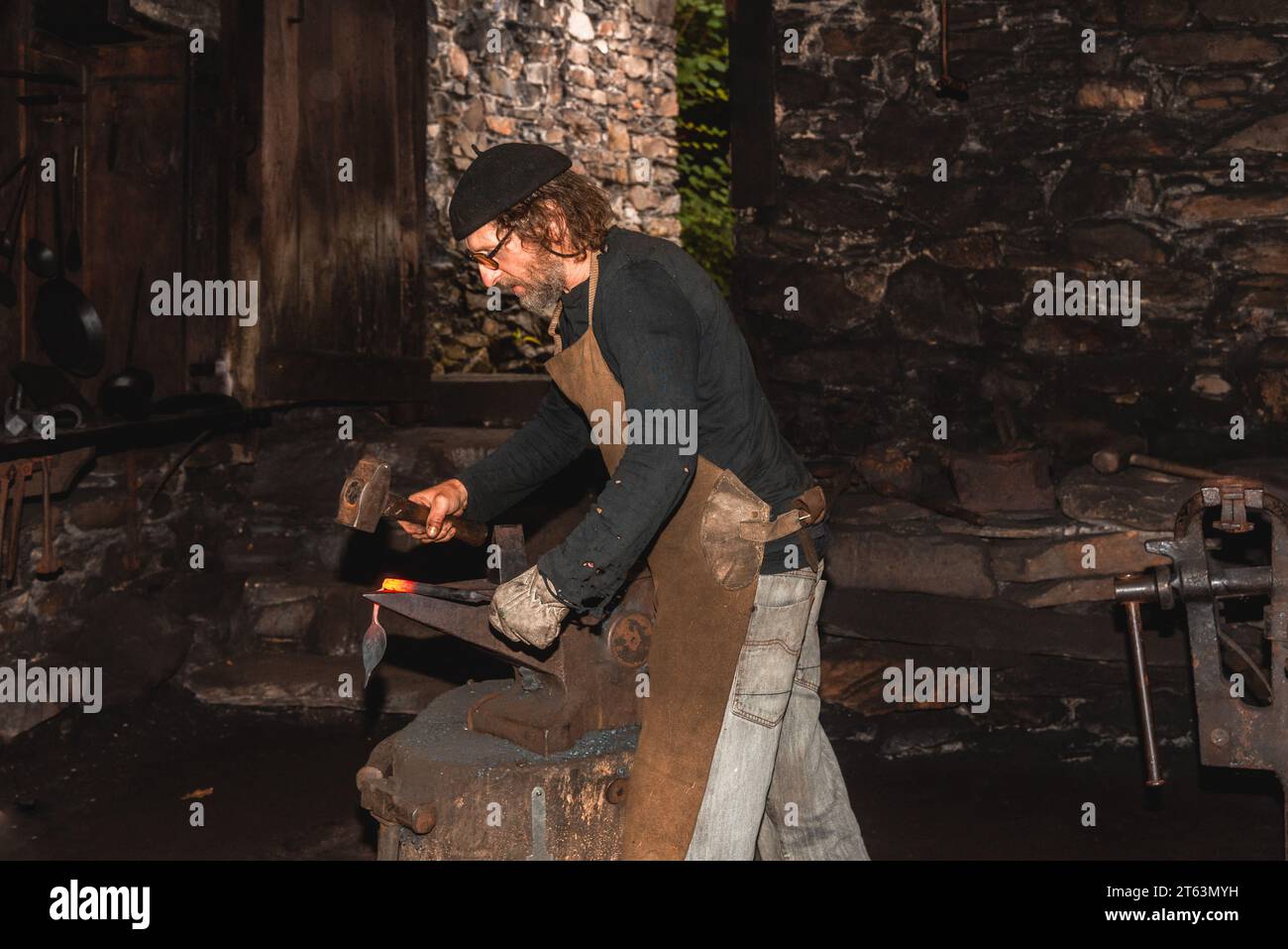 Side view of skilled blacksmith adorned in worn clothing meticulously ...