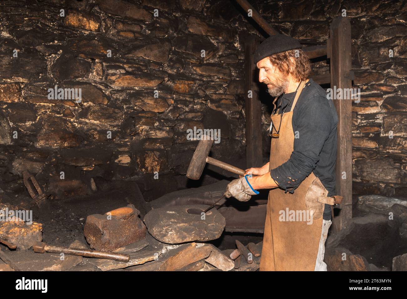 Side view of focused blacksmith in a rustic workshop, holding a hammer ...