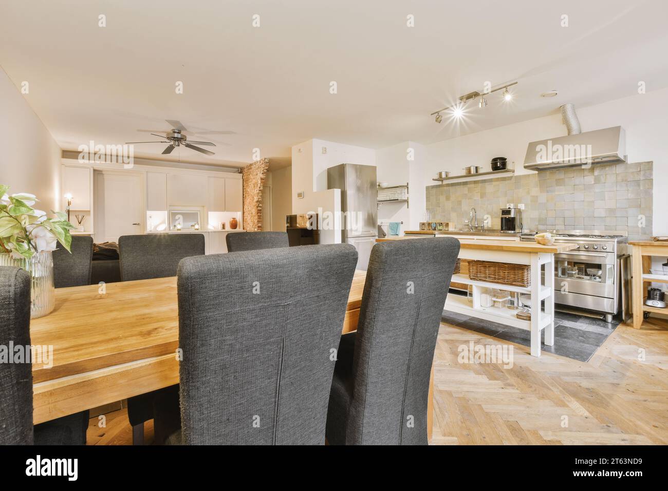 Wooden dining table with chairs arranged in front of open plan kitchen ...