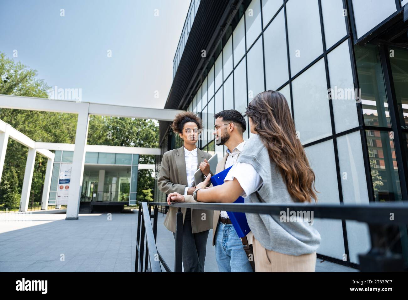 Three business people waiting in front of office building taking a ...