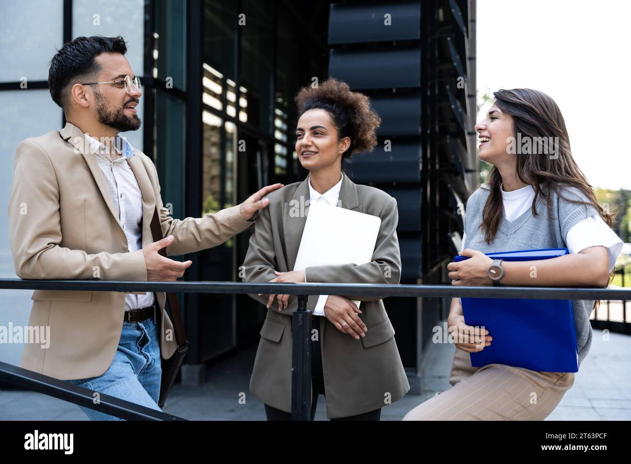 Three business people waiting in front of office building taking a ...
