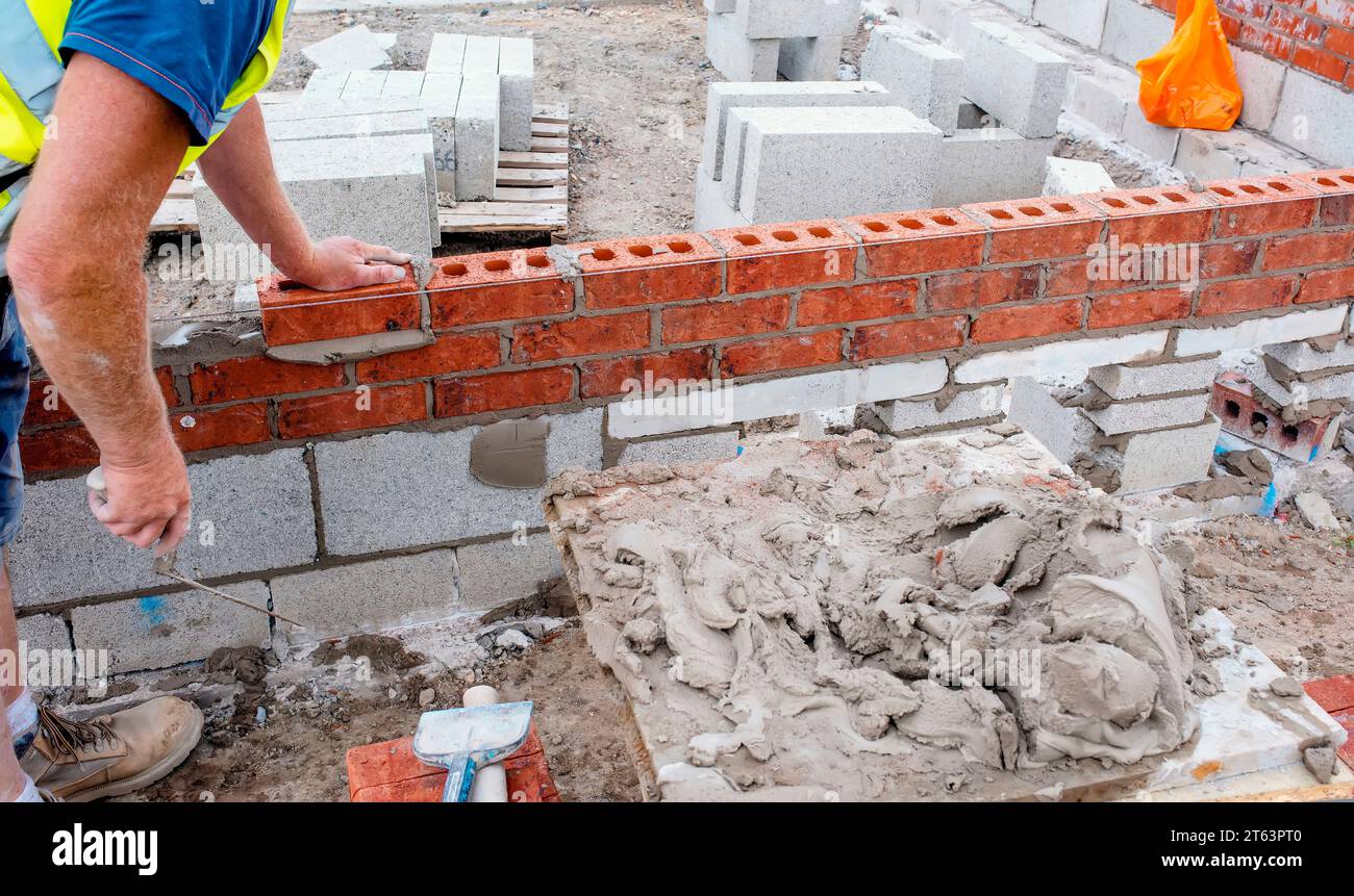 Hard working bricklayer lays bricks on cement mix on construction site ...