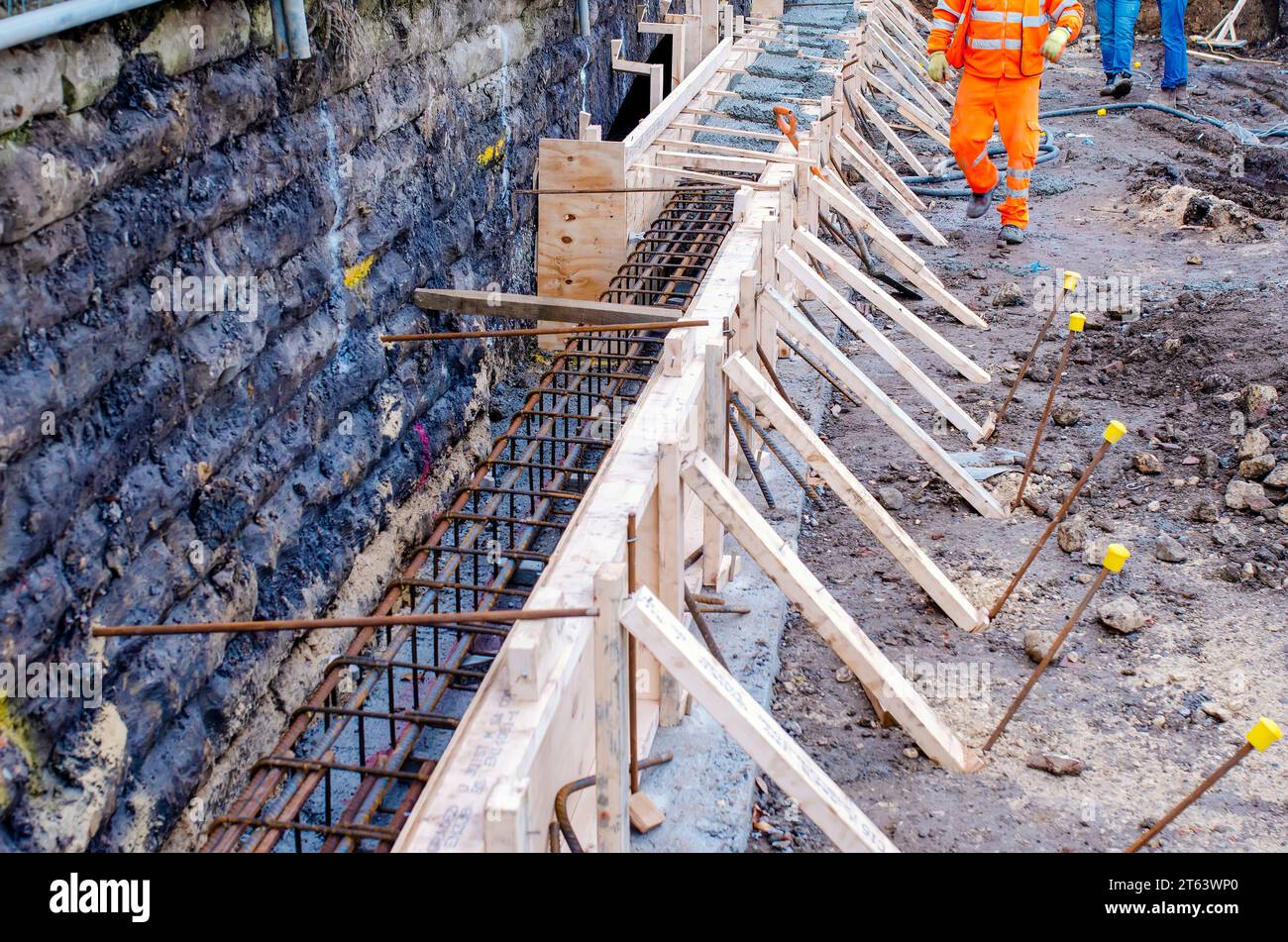 Builders pouring wet ready-mix concrete into formwork along the footing of an old bridge to ...