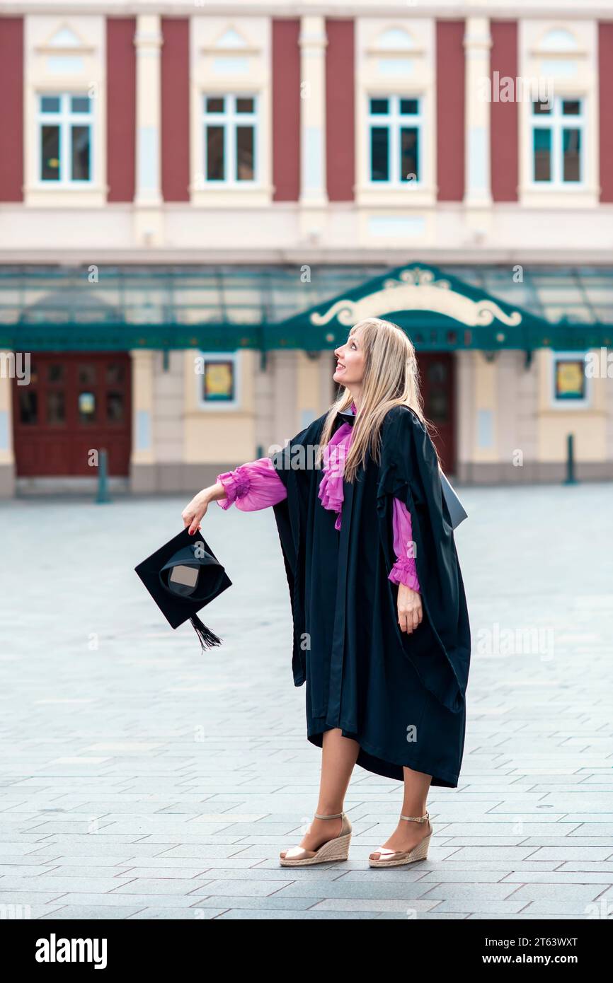 forty-year-old happy woman in a graduation gown walking around the city ...