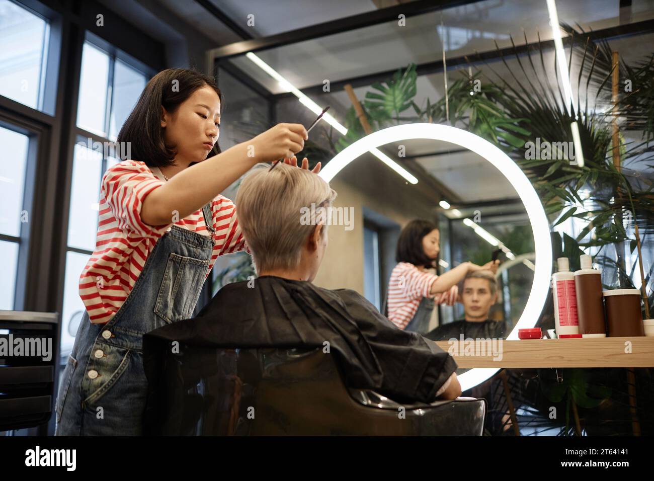 Side view portrait of young Asian woman styling hair of male client in ...
