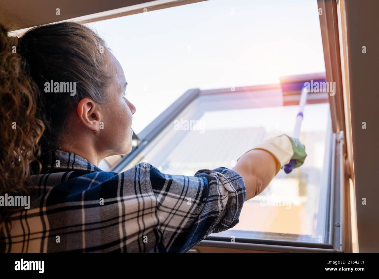 Brunette woman cleaning roof light window at home using squeegee Stock ...