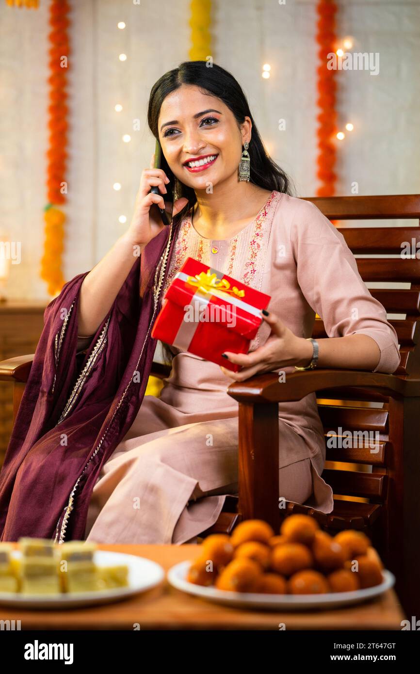 Vertical shot of indian girl talking on mobile phone by holding gift ...