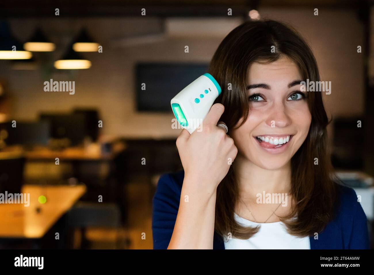 Caucasian woman holding an infrared thermometer to her temple like a ...