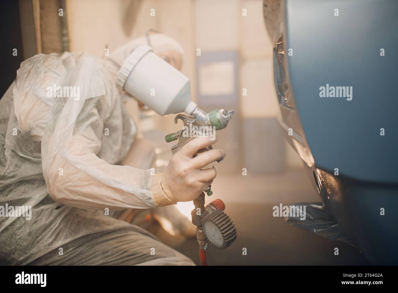 Car painter in protective clothes and respirator mask painting vehicle ...