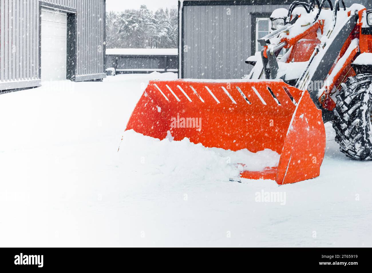 Little red tractor with snowplow removing snow during snowfall ...
