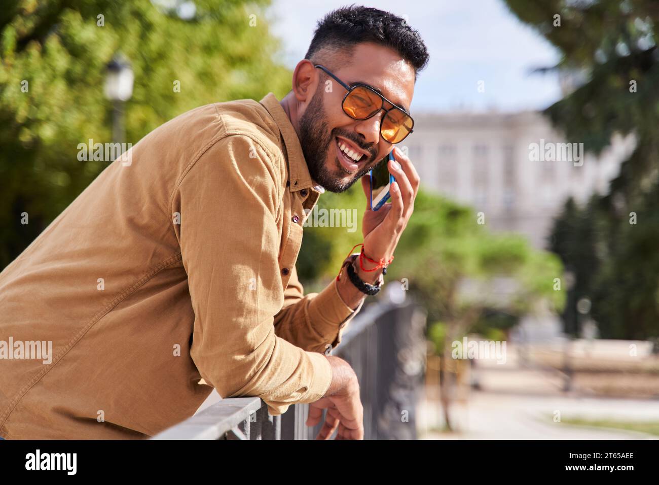 Smiling man leaning on a railing talking on his cell phone. young ...