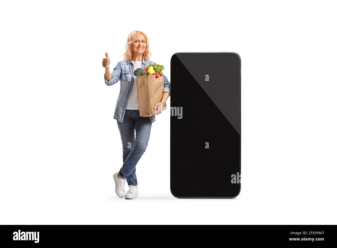 Woman with a grocery bag leaning on a big mobile phone and gesturing ...