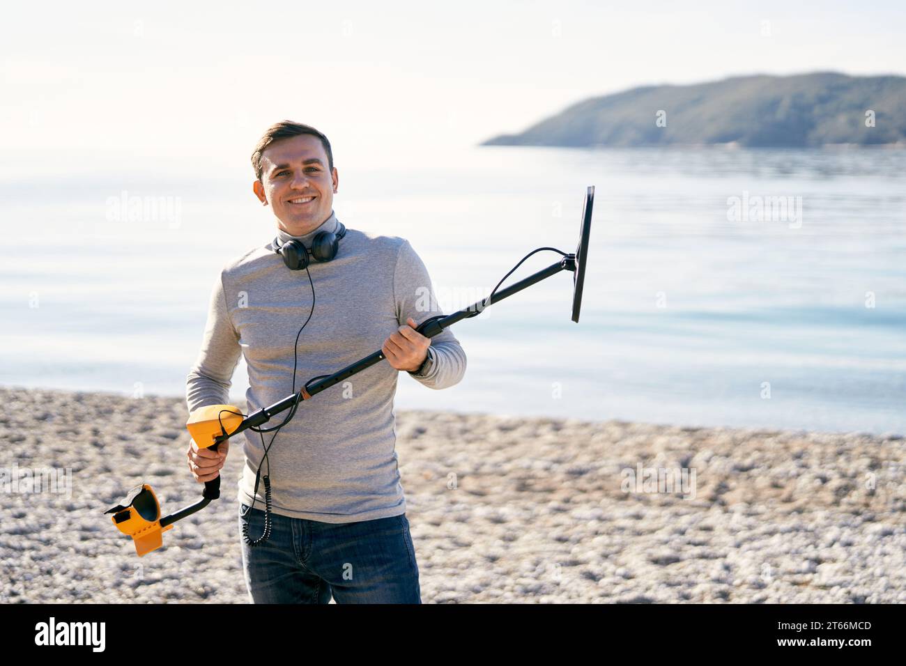 Smiling man with a metal detector at the ready stands by the sea Stock ...