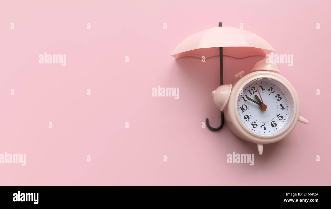 Clock under an umbrella. Concept of protection time. Pink background ...