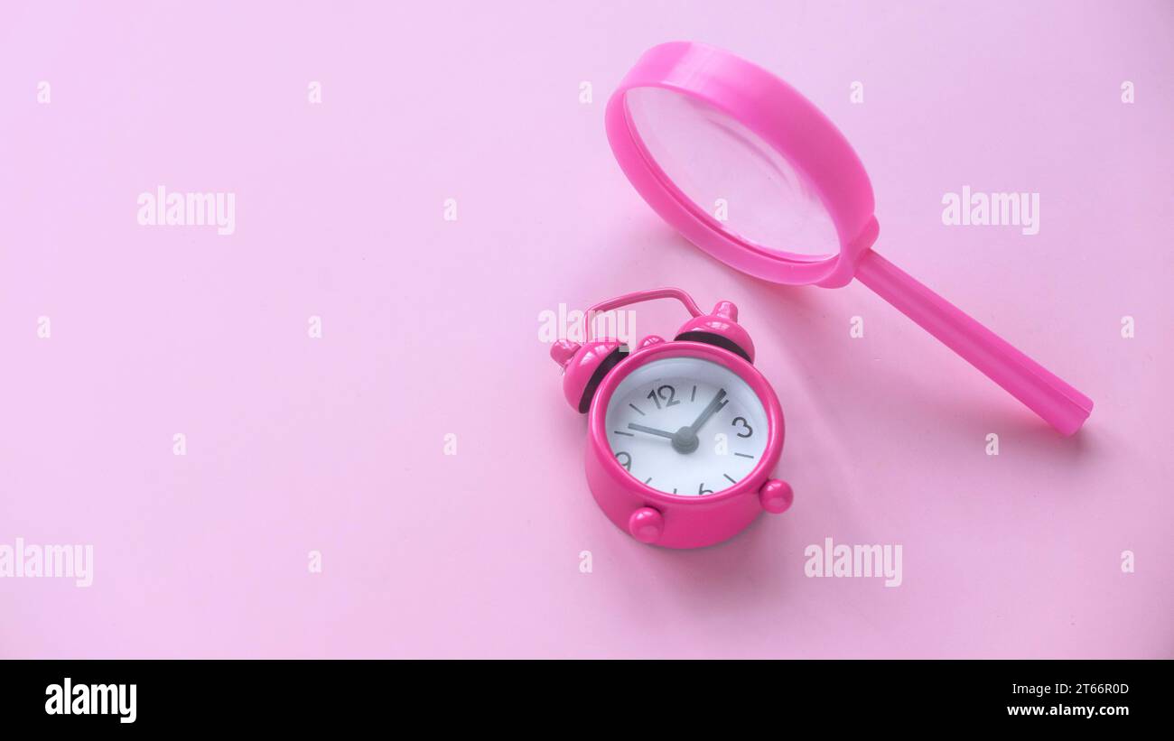 Pink alarm clock and magnifying glass on a pink background with copy ...