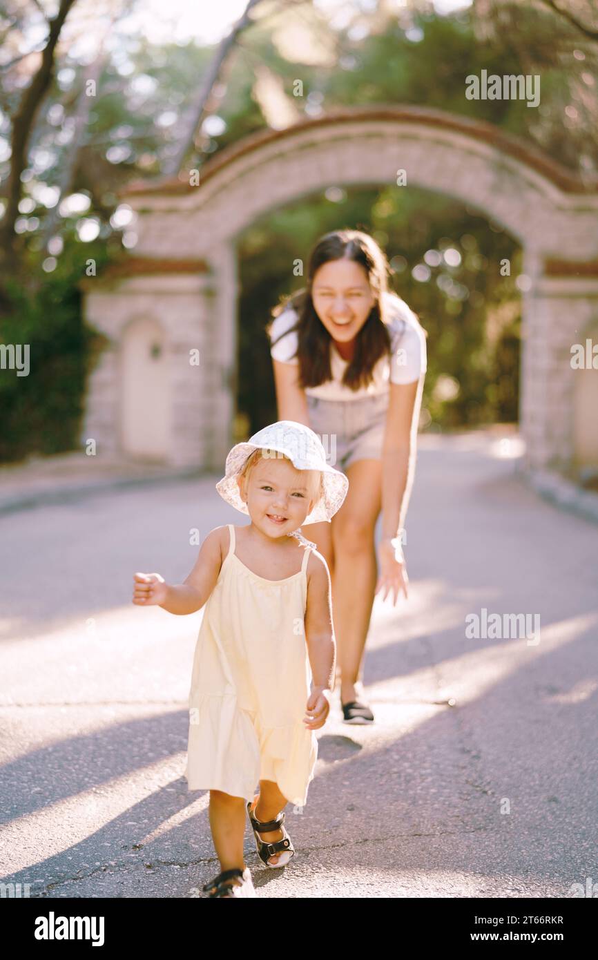 Laughing mom chasing little girl down the road in the park Stock Photo ...
