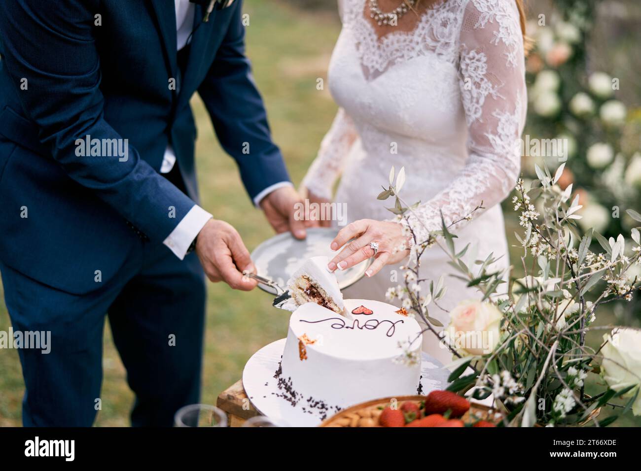 Bride and groom put a piece of wedding cake on a plate. Cropped ...