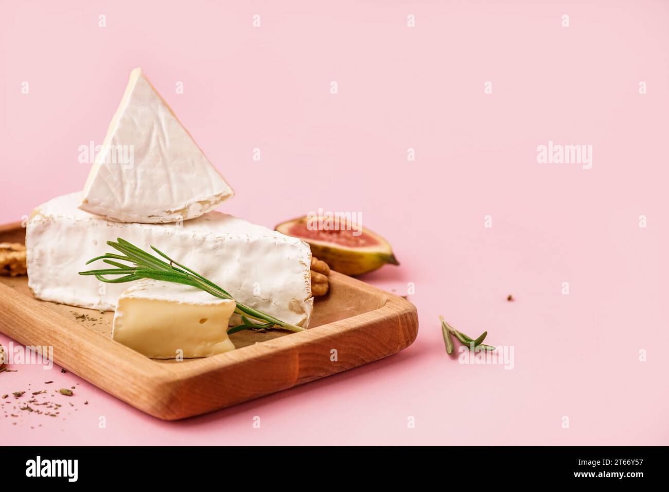 Wooden board with pieces of tasty Camembert cheese on pink background ...