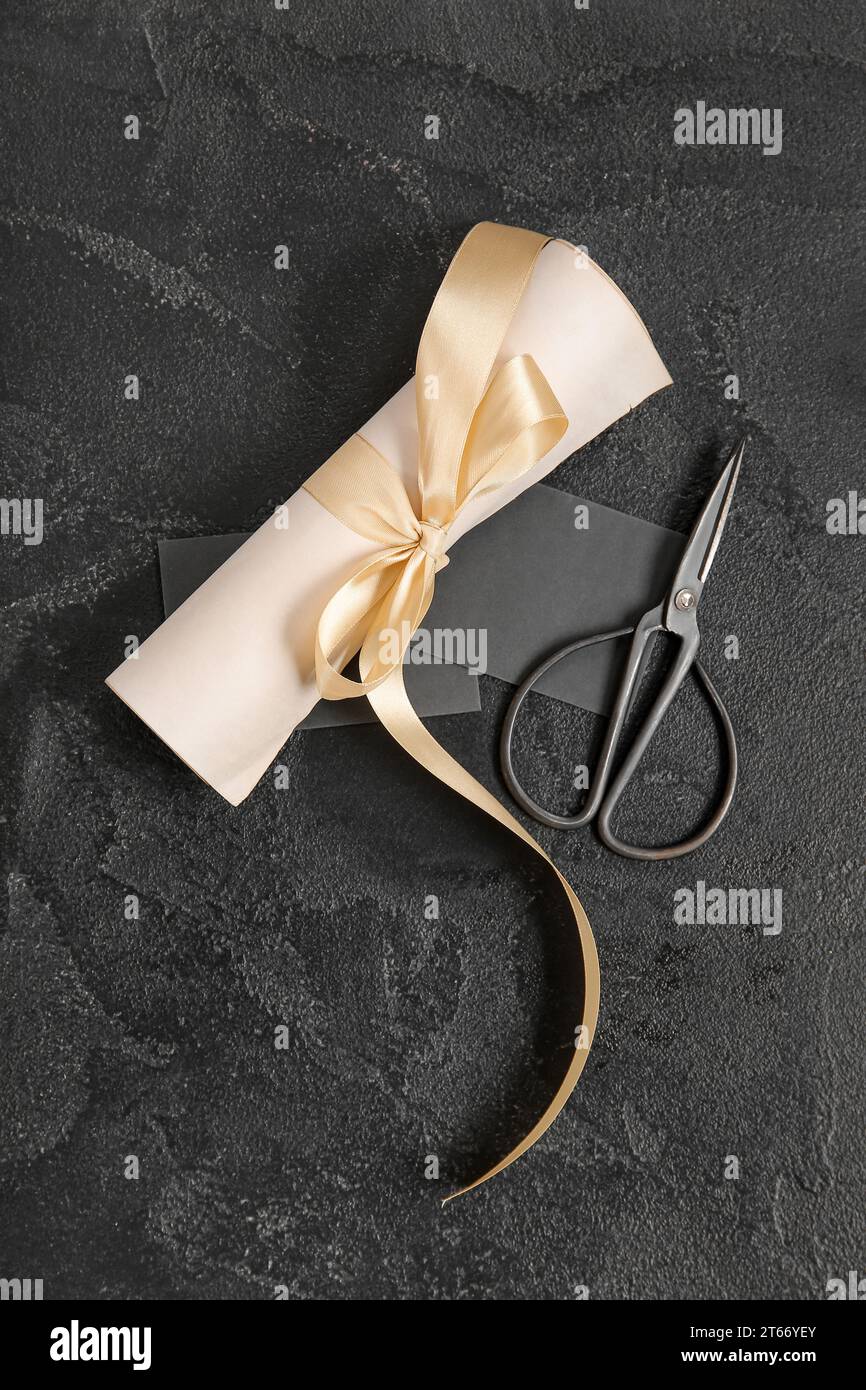 Roll of paper tied with golden ribbon and scissors on black background ...
