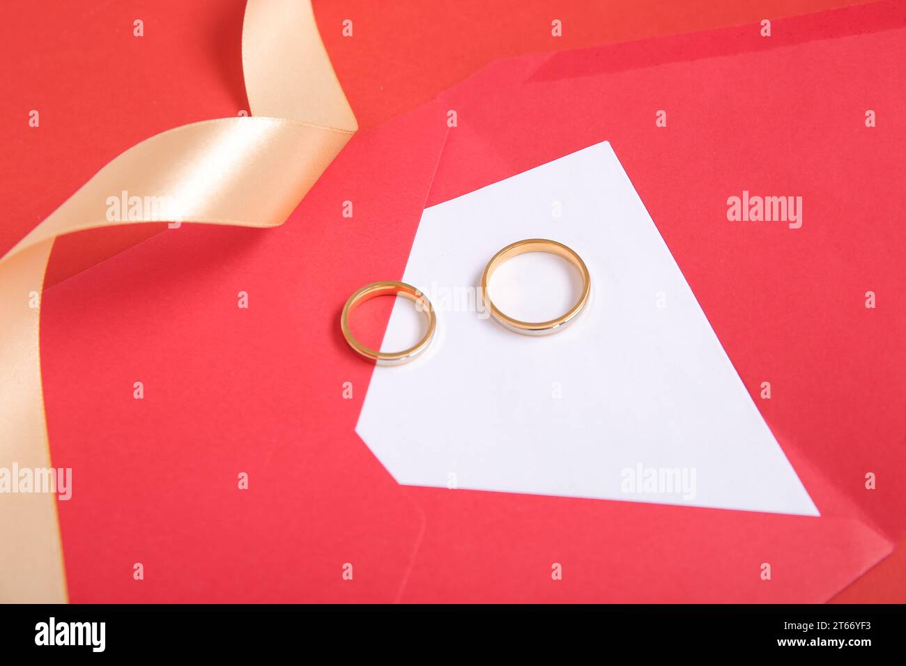 Envelope with greeting card, rings and golden ribbon on red background ...