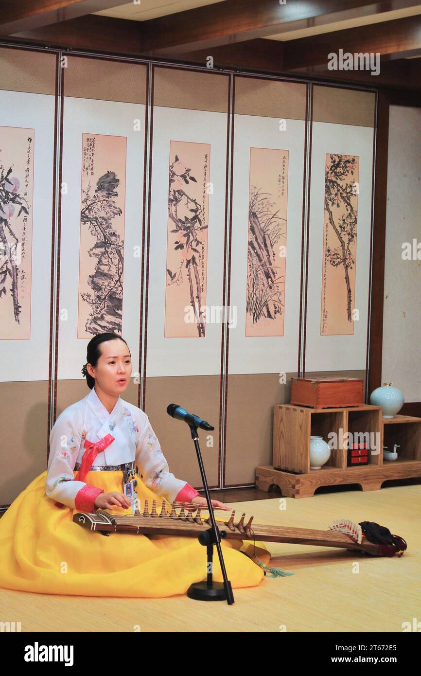 A woman wearing colorful hanbok clothing plays a gayageum, a ...