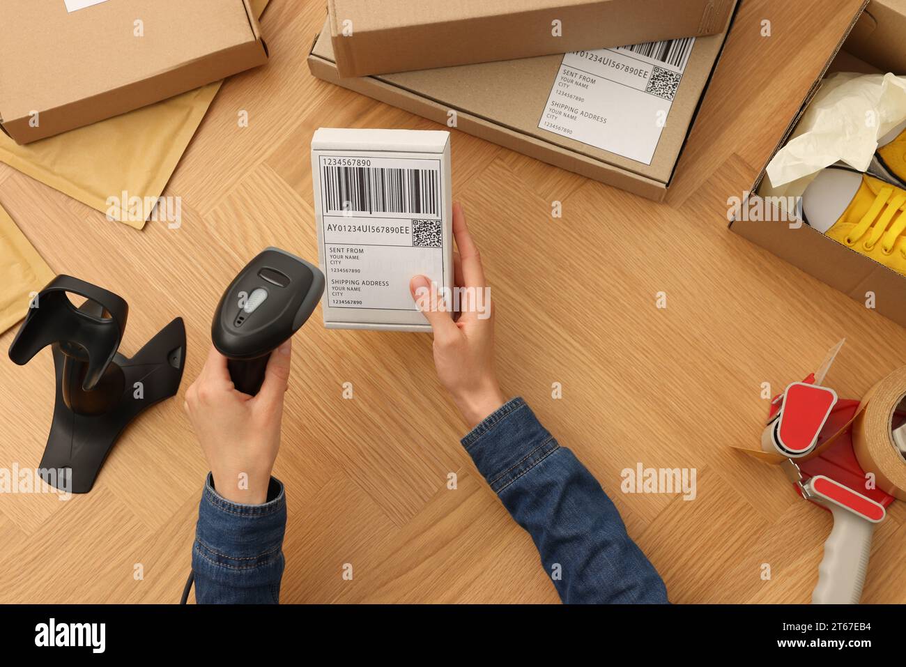 Woman with scanner reading parcel barcode at wooden table, top view ...