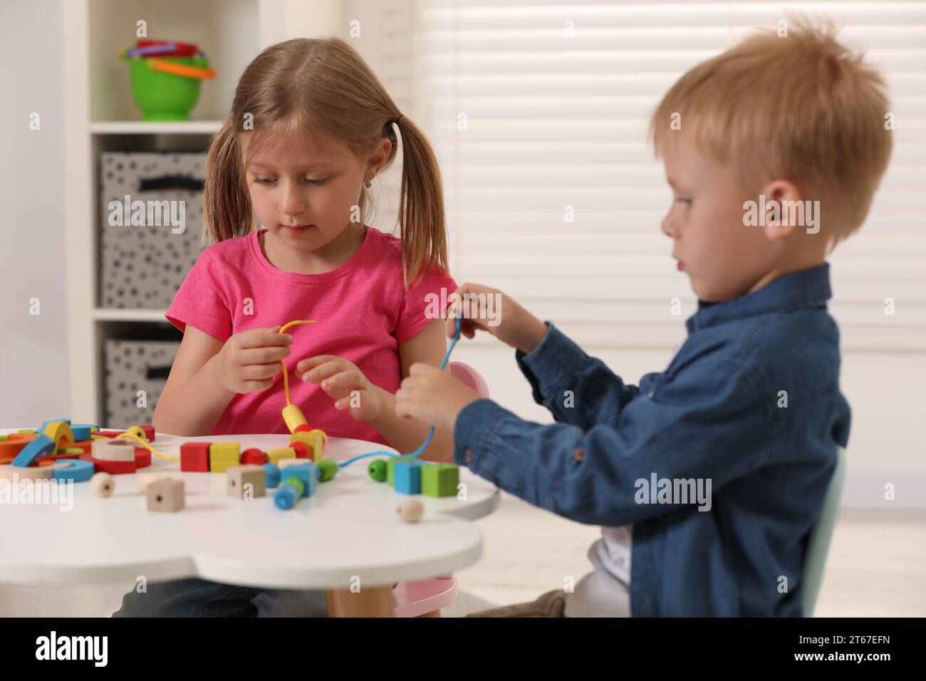 Little children playing with wooden pieces and string for threading ...