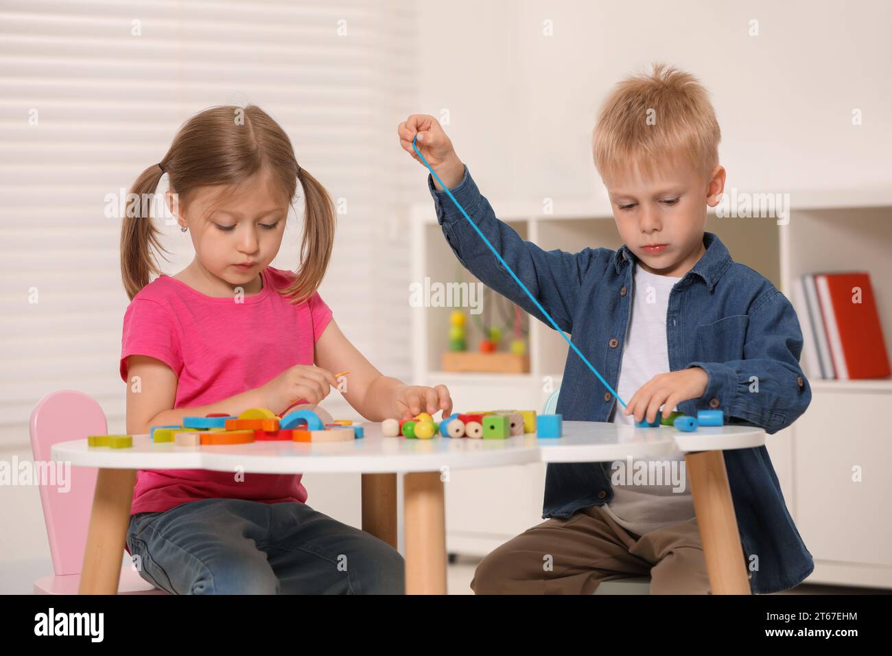 Little children playing with wooden pieces and string for threading ...