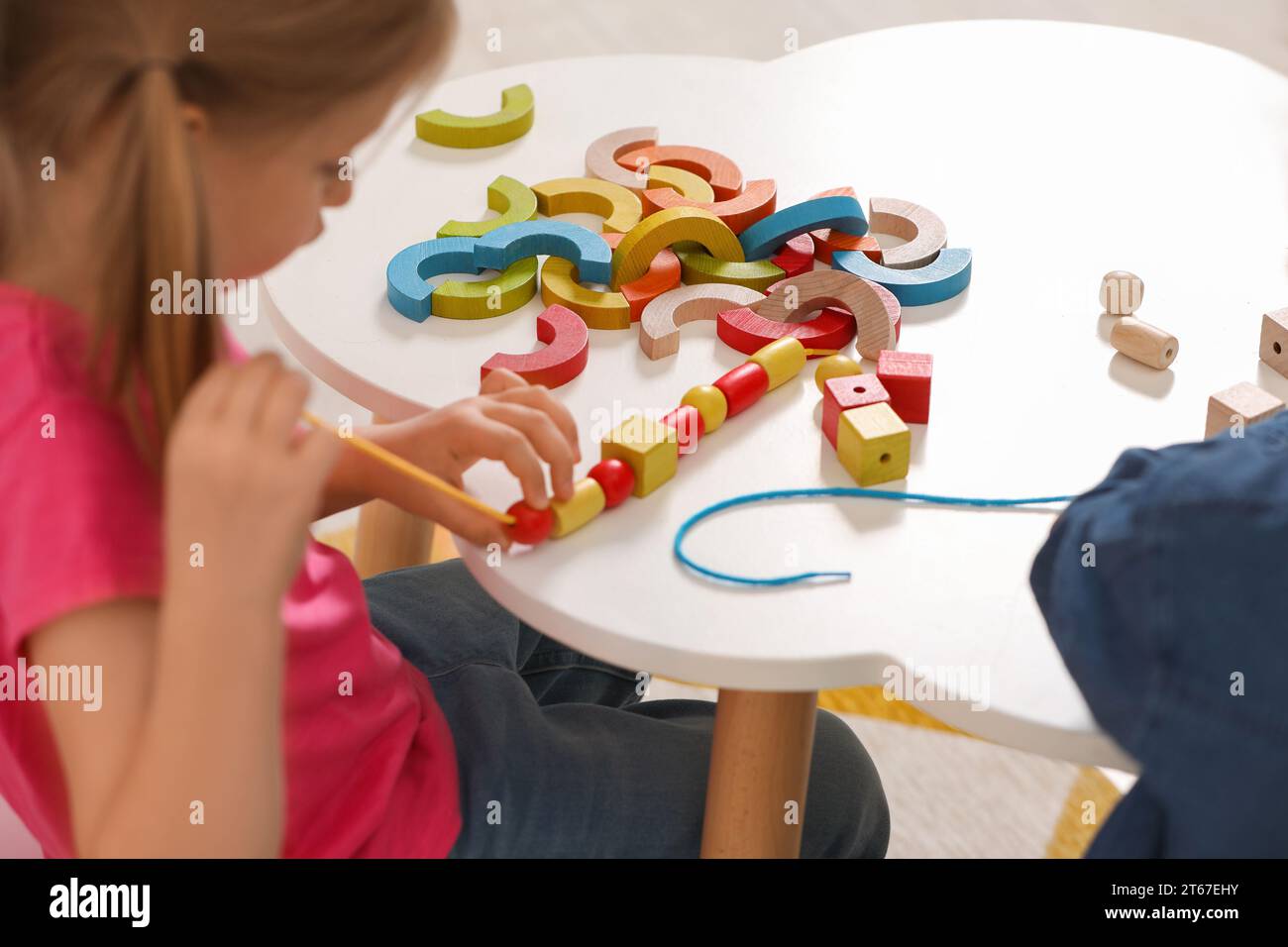 Little children playing with wooden pieces and string for threading ...