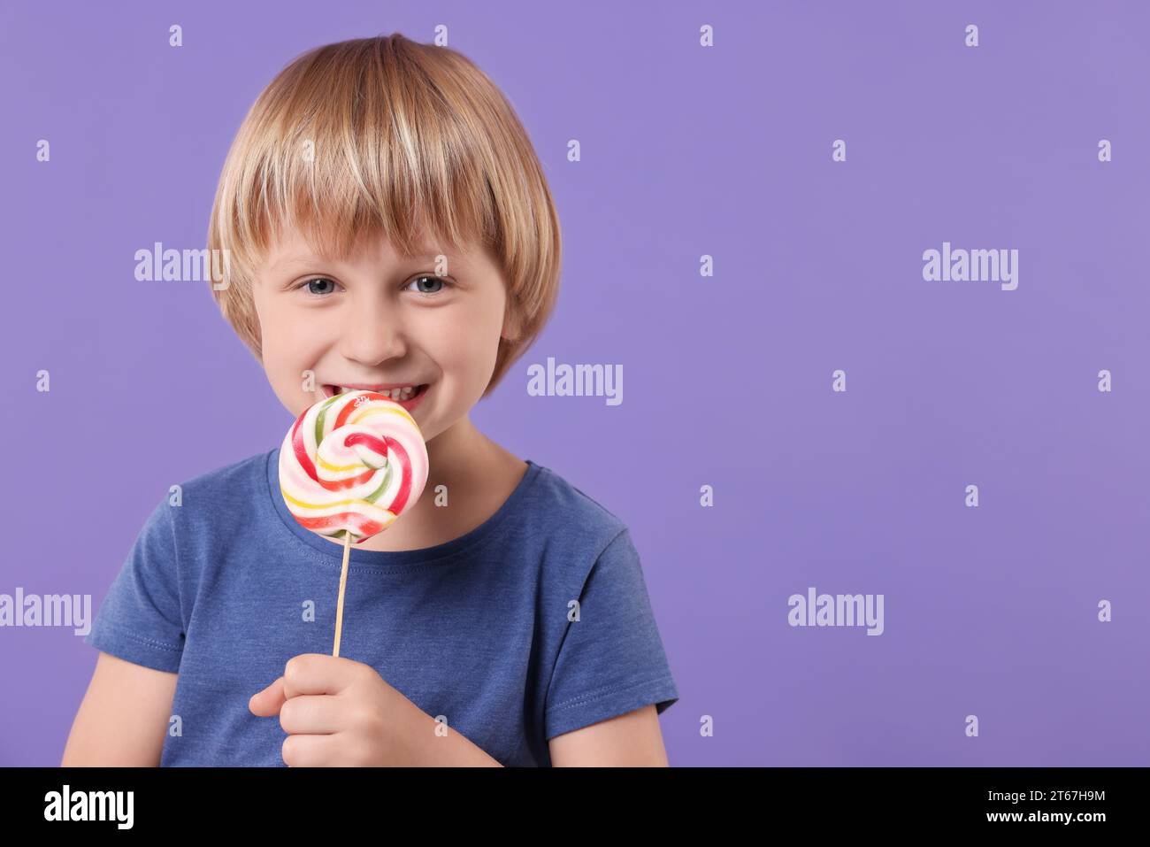Happy little boy licking colorful lollipop swirl on violet background ...