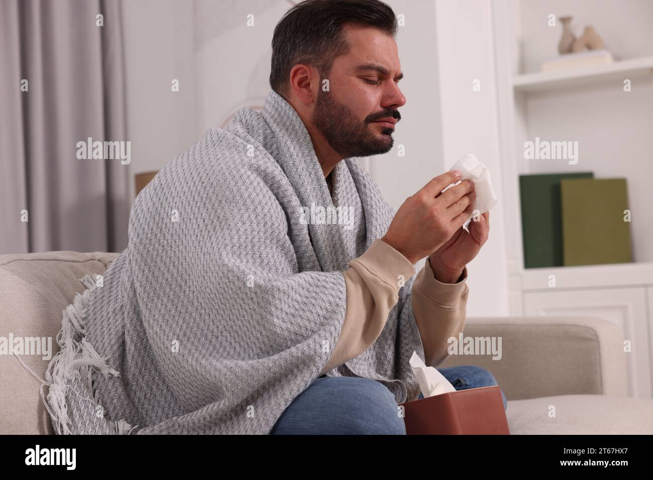 Sick man wrapped in blanket with tissues on sofa at home. Cold symptoms ...