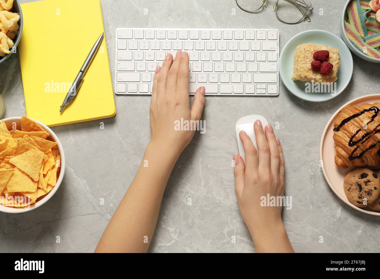 Bad eating habits. Woman working on computer at light grey marble table ...