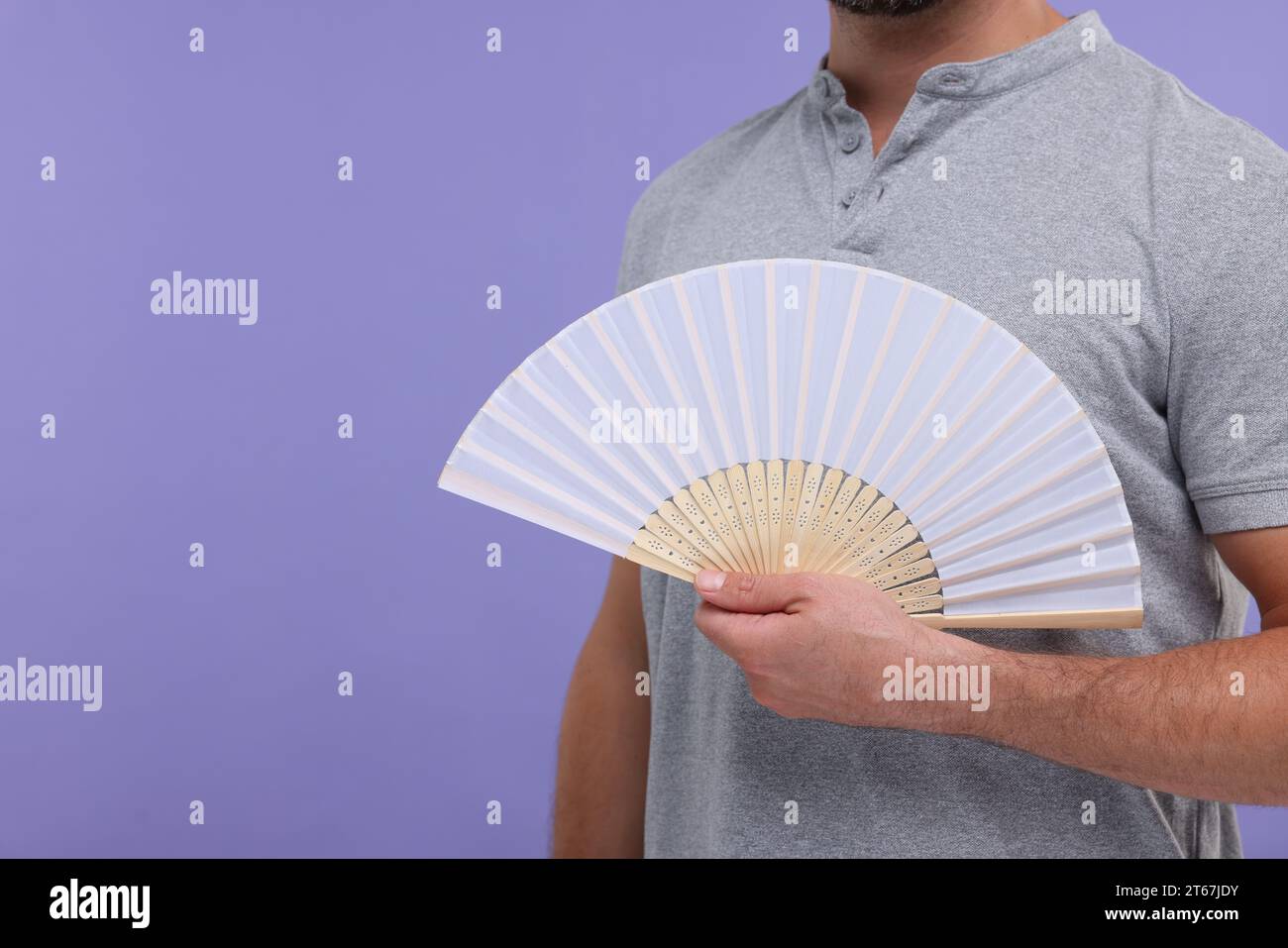 Man holding hand fan on purple background, closeup. Space for text ...
