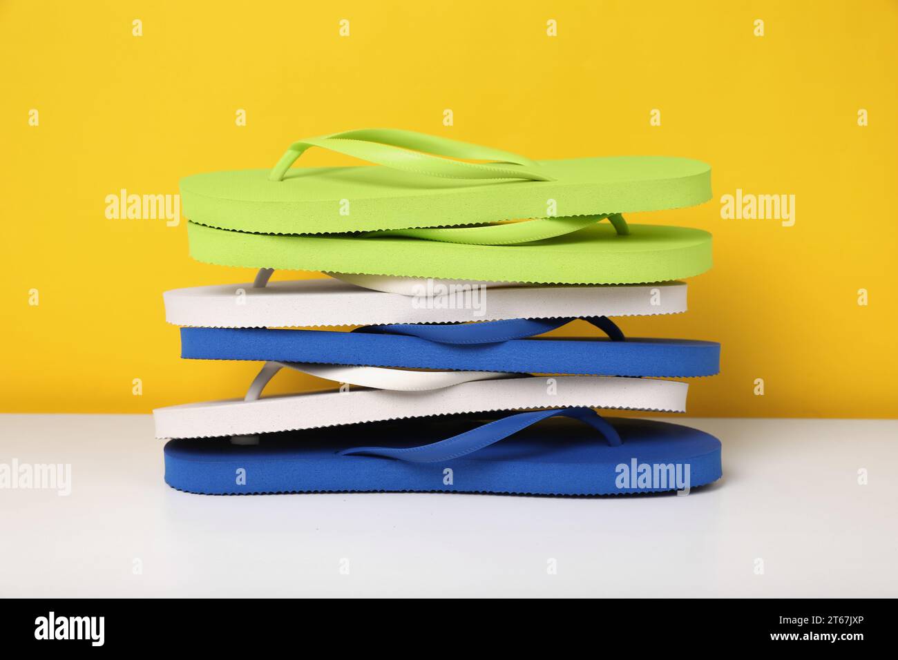 Stack of different flip flops on white table against yellow background ...
