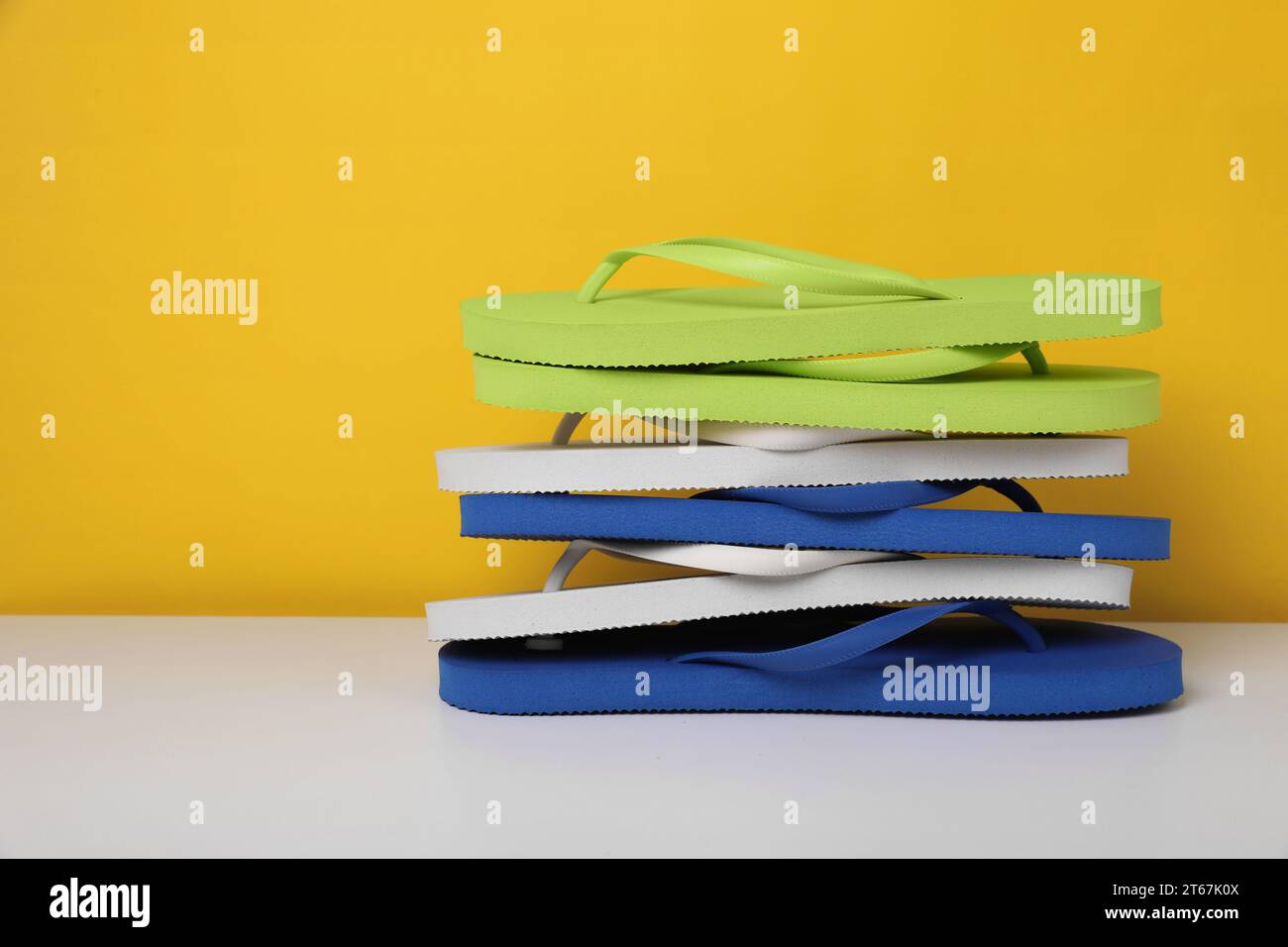 Stack of different flip flops on white table against yellow background ...