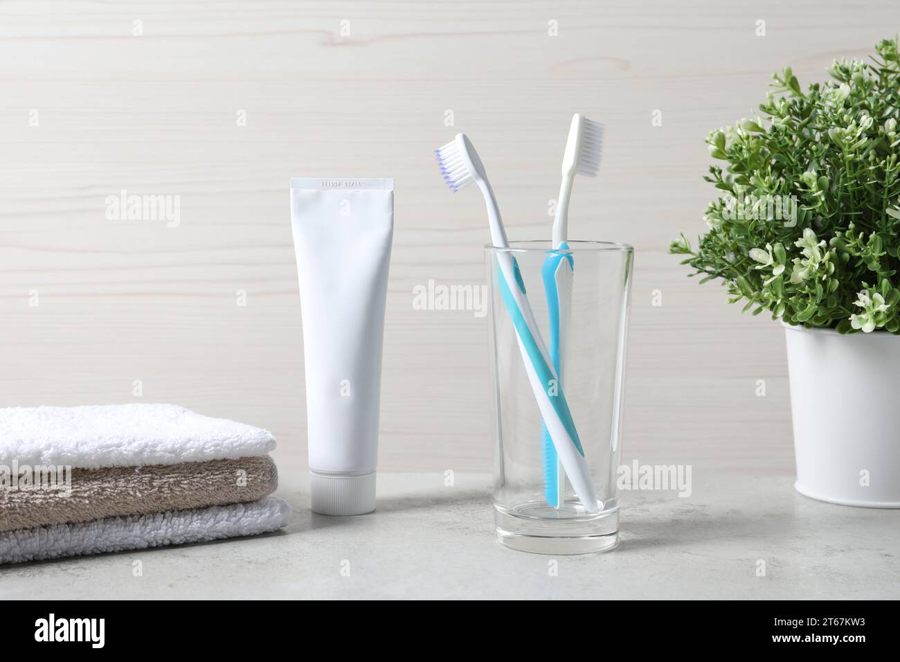 Plastic toothbrushes in glass holder, tube of toothpaste and towels on ...