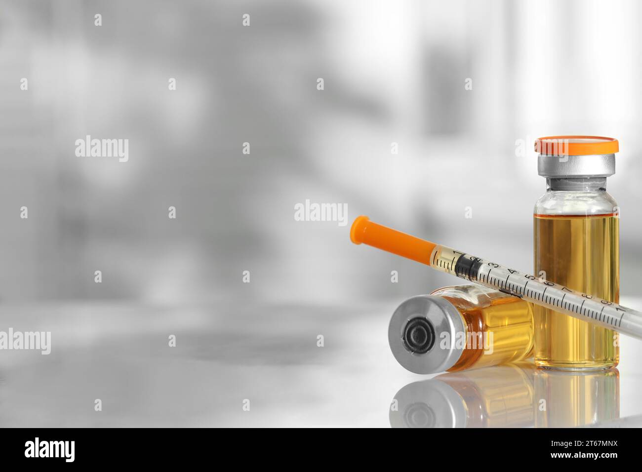 Glass vials and syringe with orange medication on white table, closeup ...
