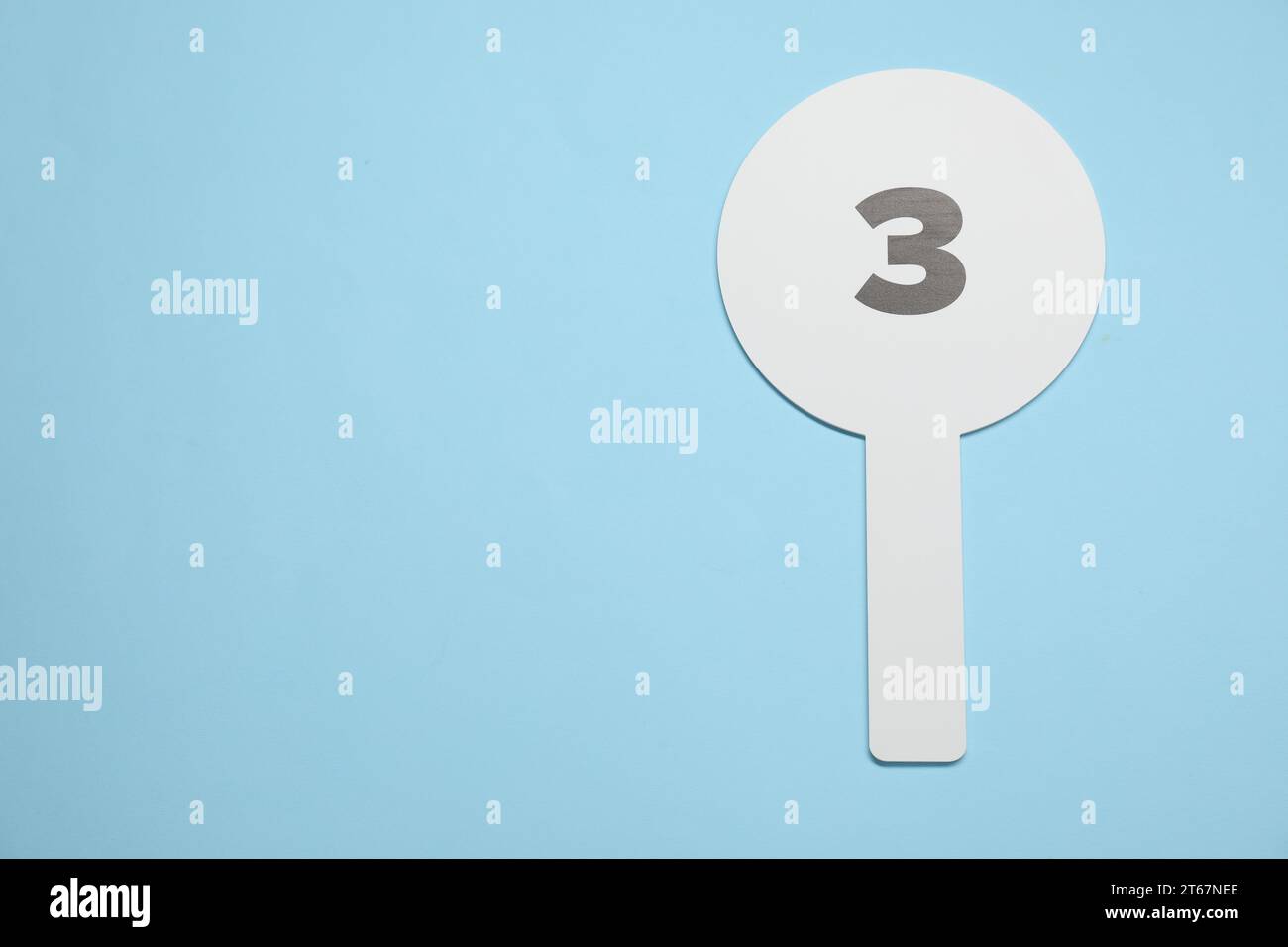Auction paddle with number 3 on light blue background, top view. Space ...
