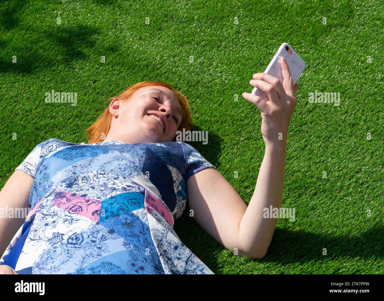 Woman with red/ginger hair in a blue and pink patterned dress lying on ...